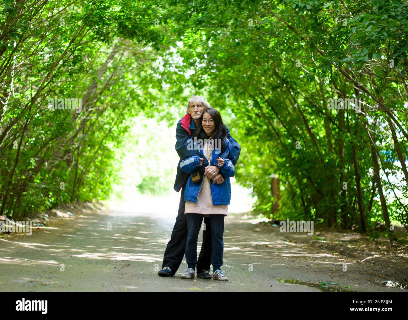 Adult male friendly hugs a young girl in an alley with trees Stock ...