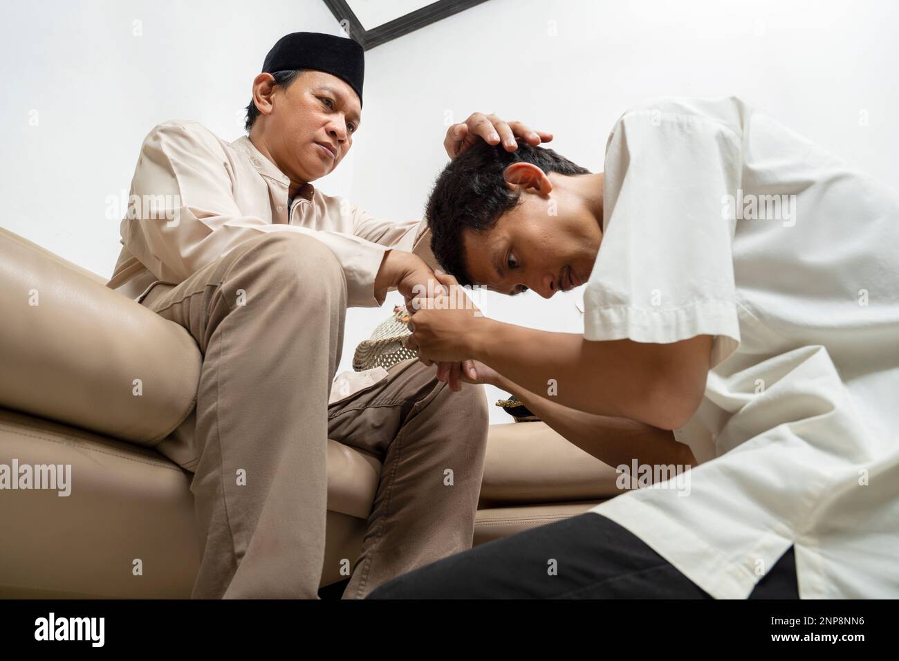 Asian Muslim man asking forgiveness from his father at home. Sungkem is ...
