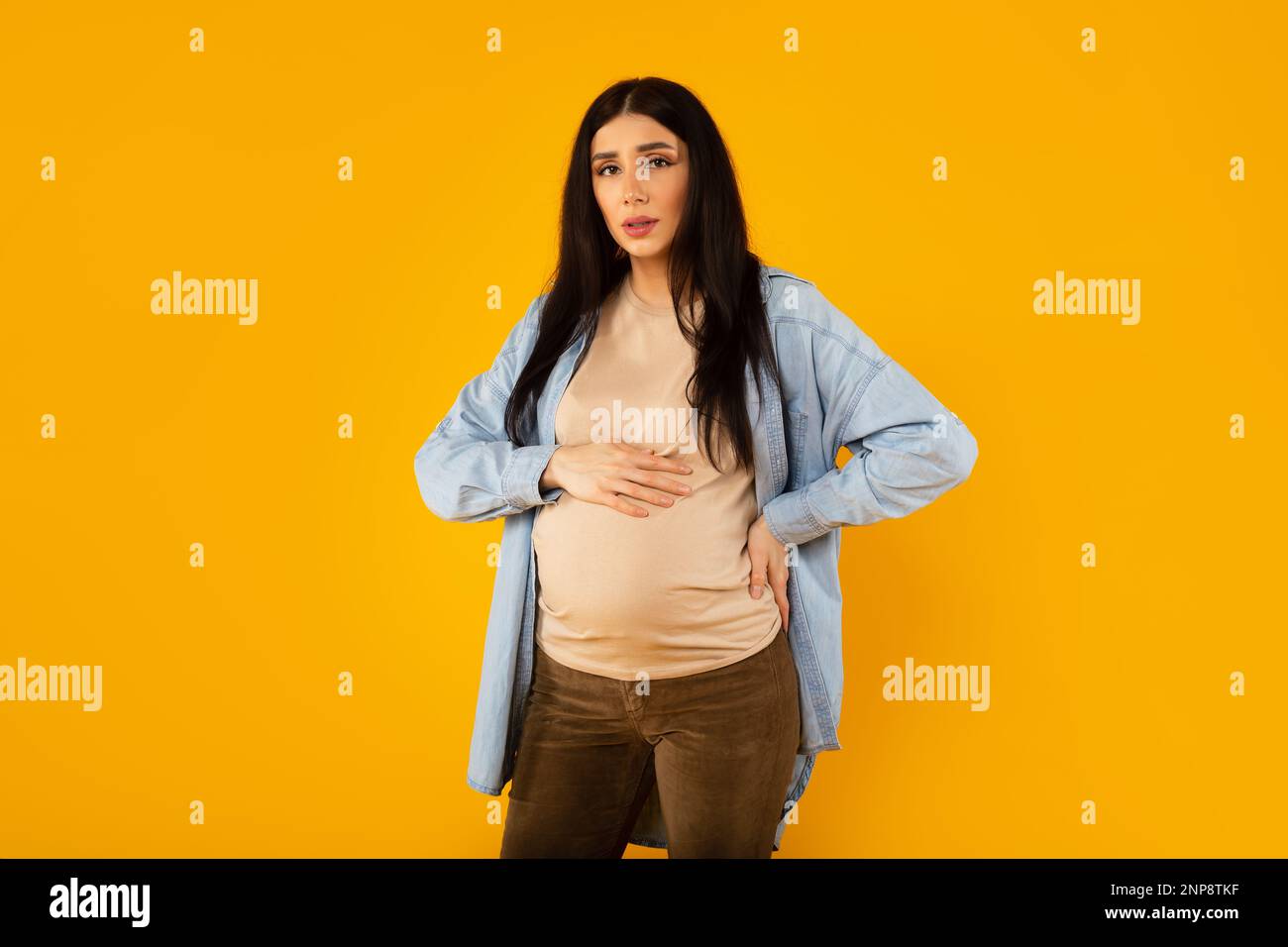 Sad young pregnant woman having back pain, touching belly and ache zone ...