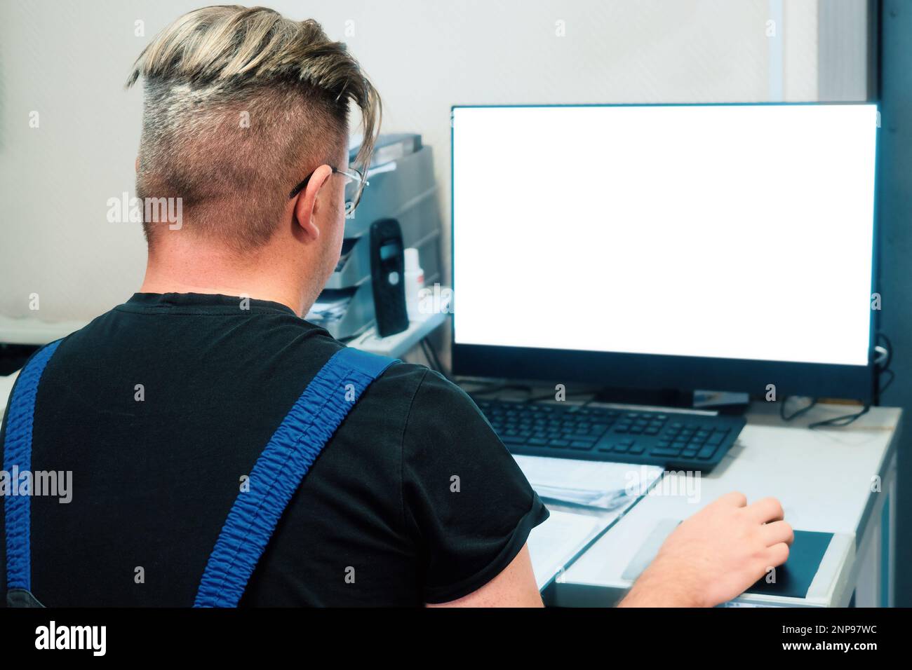 Working man sits at desk and looks at computer monitor. View from back ...