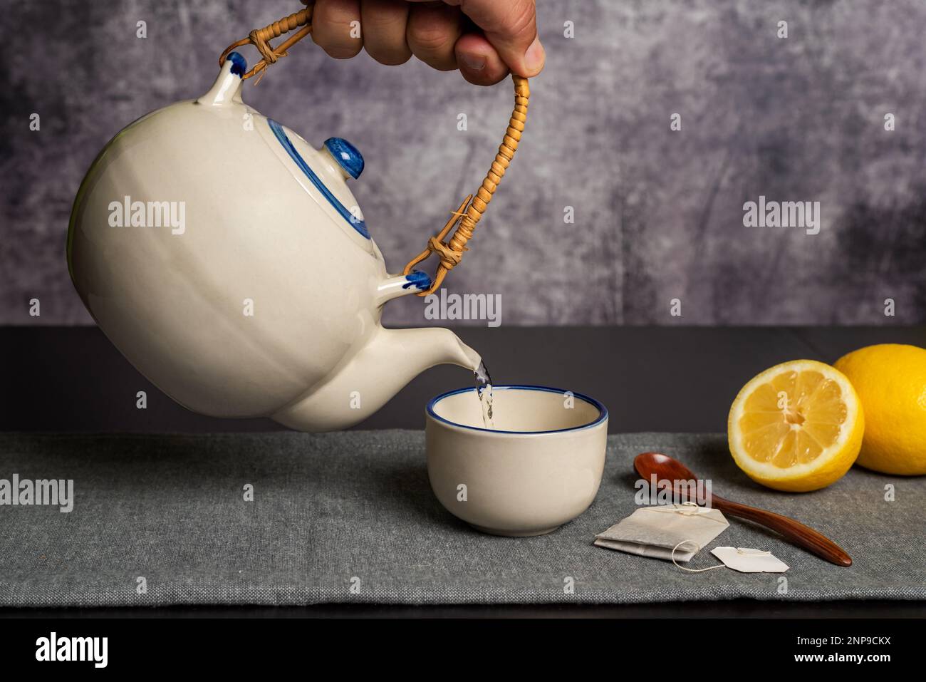 A hand holding a teapot while serving the hot water to prepare the tea ...