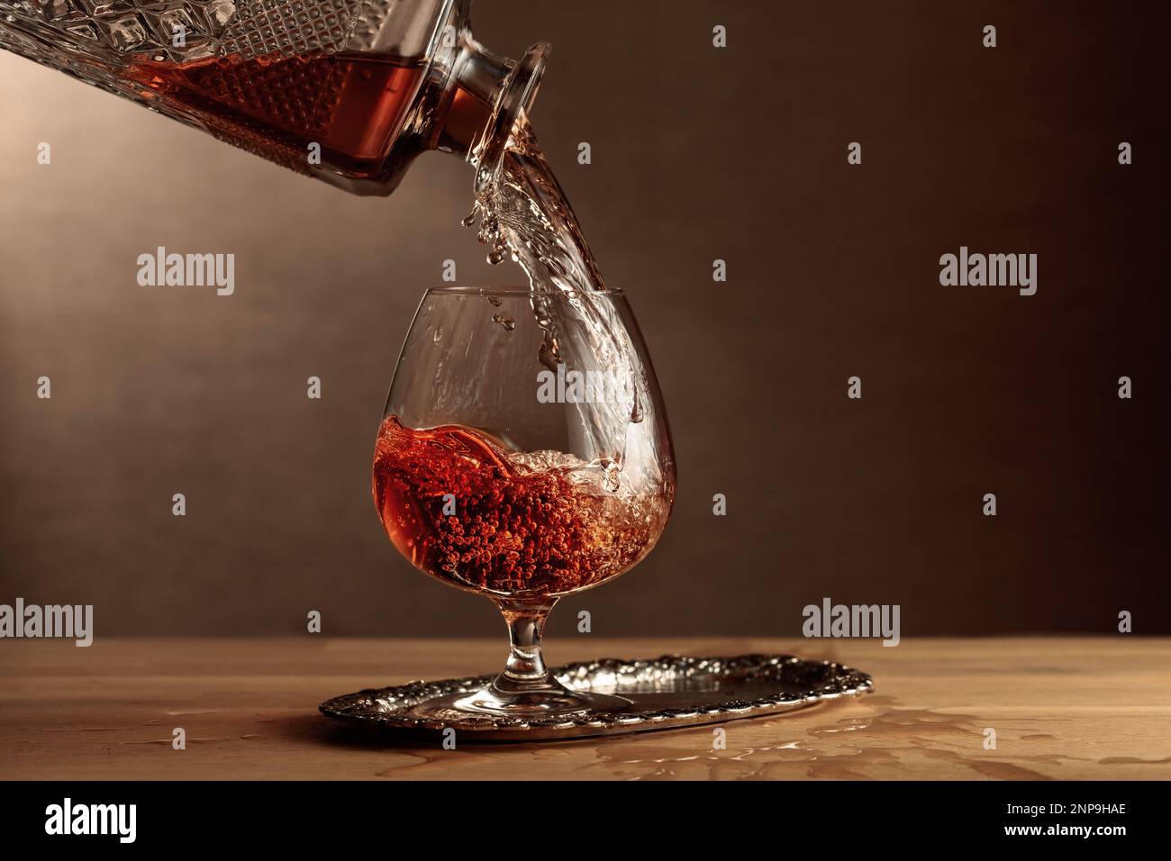 Brandy is poured from a decanter into a snifter glass. Cognac on an oak ...