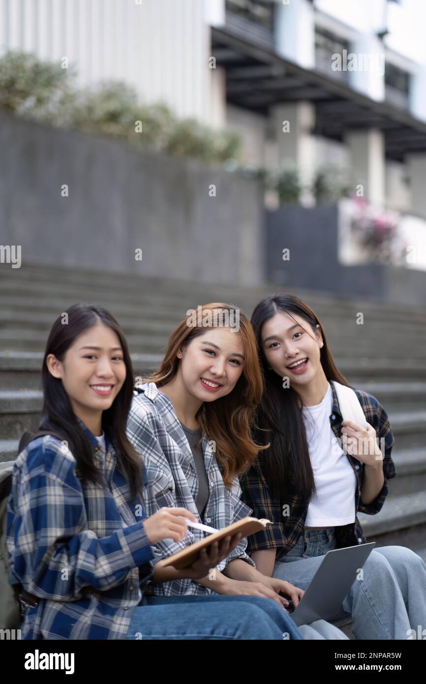 Nice young students use laptop after class sitting outdoors. girls wear ...
