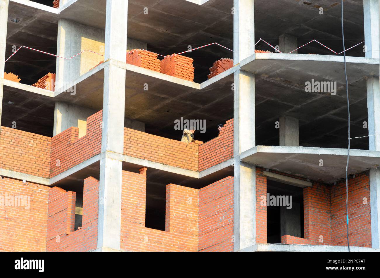 Two builders lay brick walls in a multi-apartment new house under ...
