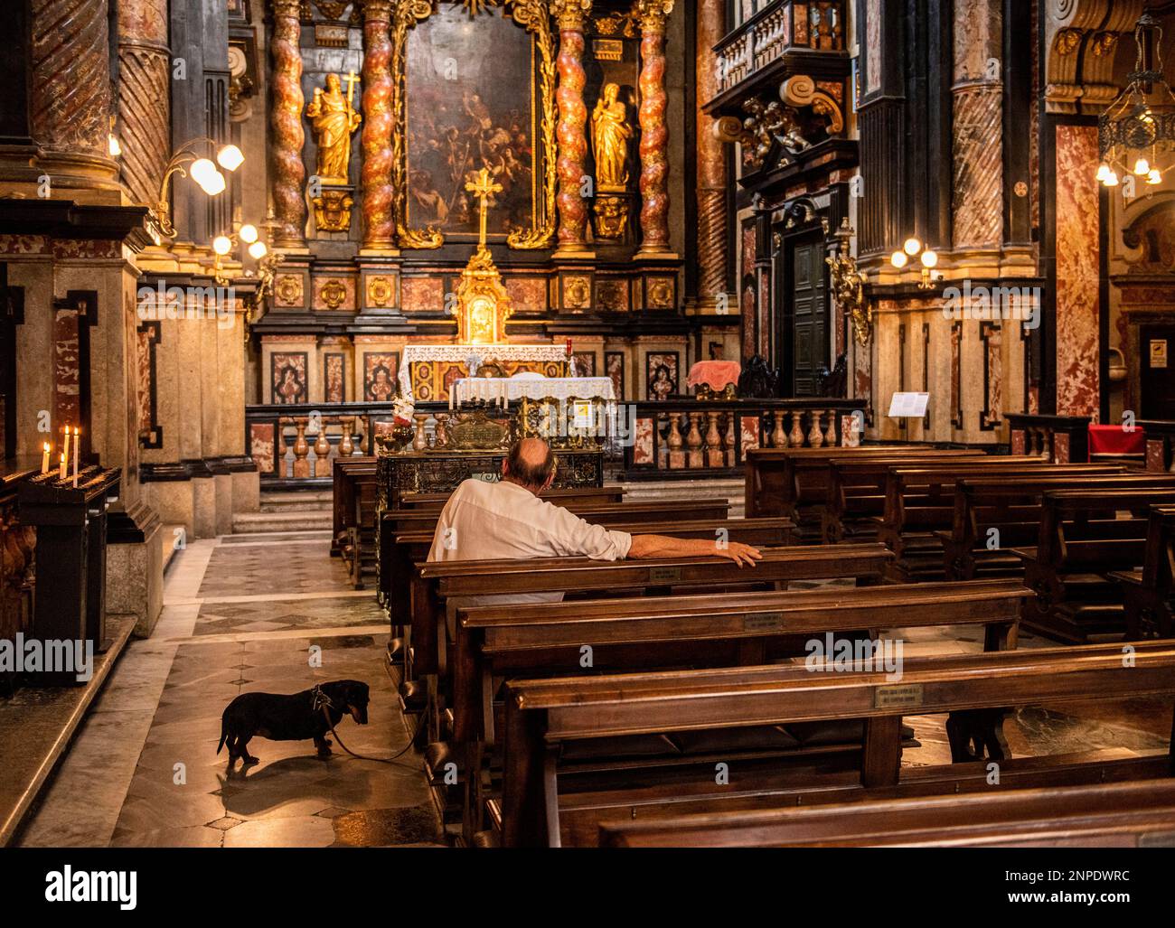A man is sitting with his dog next to him in a very ornate empty church ...