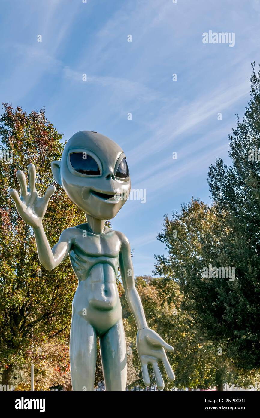 A large alien waves with a four-fingered hand, surrounded by trees ...