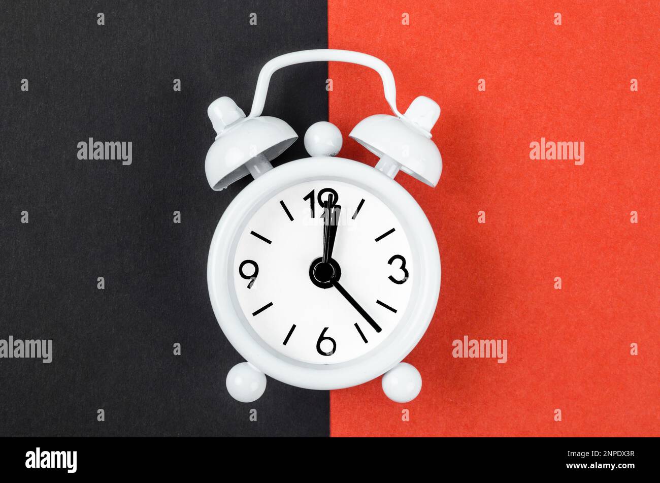 White vintage alarm clock on bright red and black colour background ...