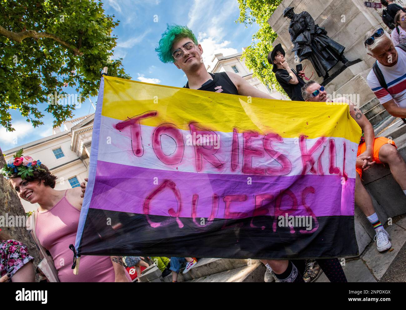 A member of the LGBTQ+ with green hair holds a banner with the words ...