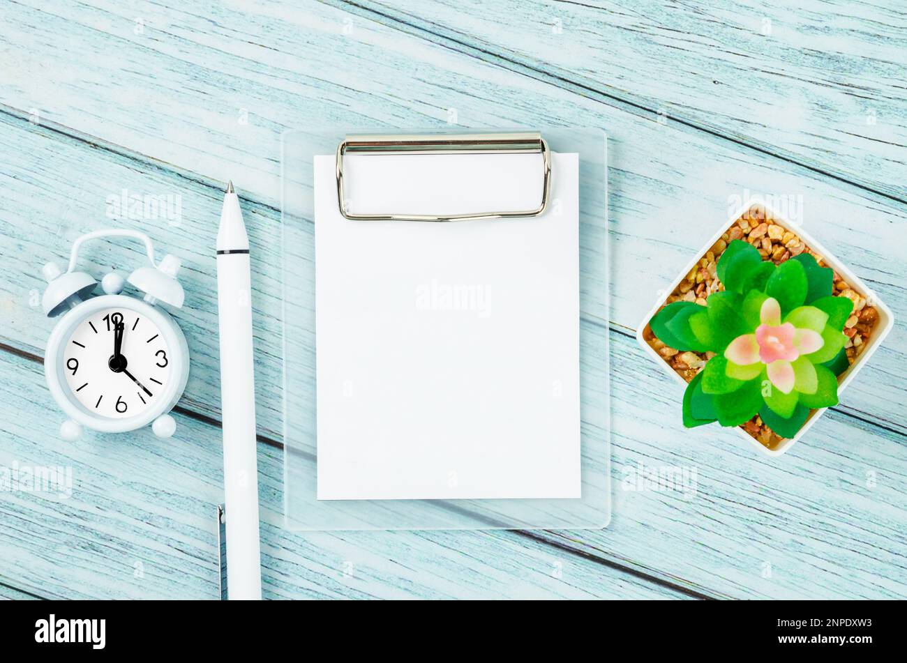 Small white paper blank page on clip board, alarm clock and pen on blue ...