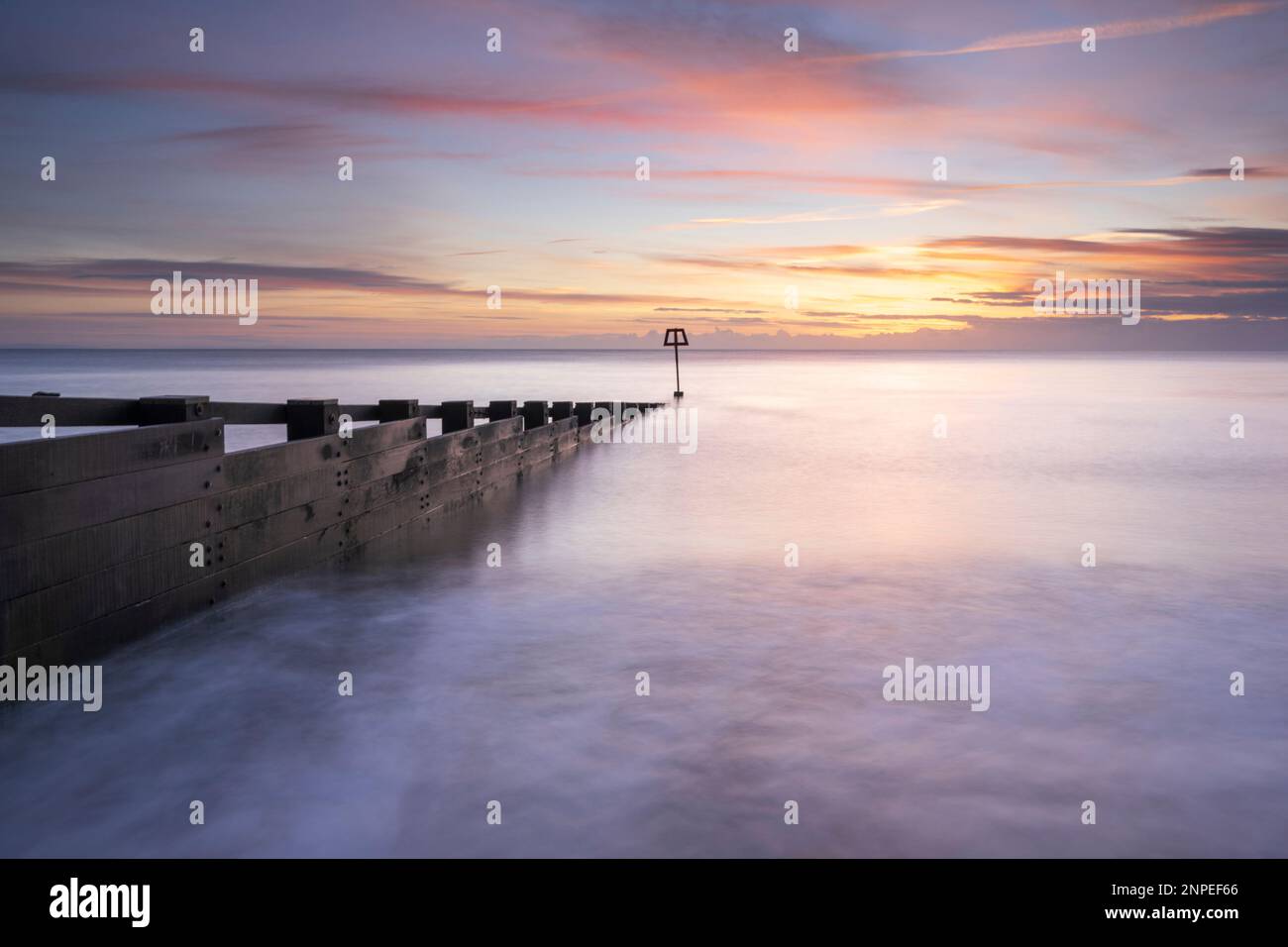 Waves washing around a groyne on a beach at sunrise Stock Photo - Alamy