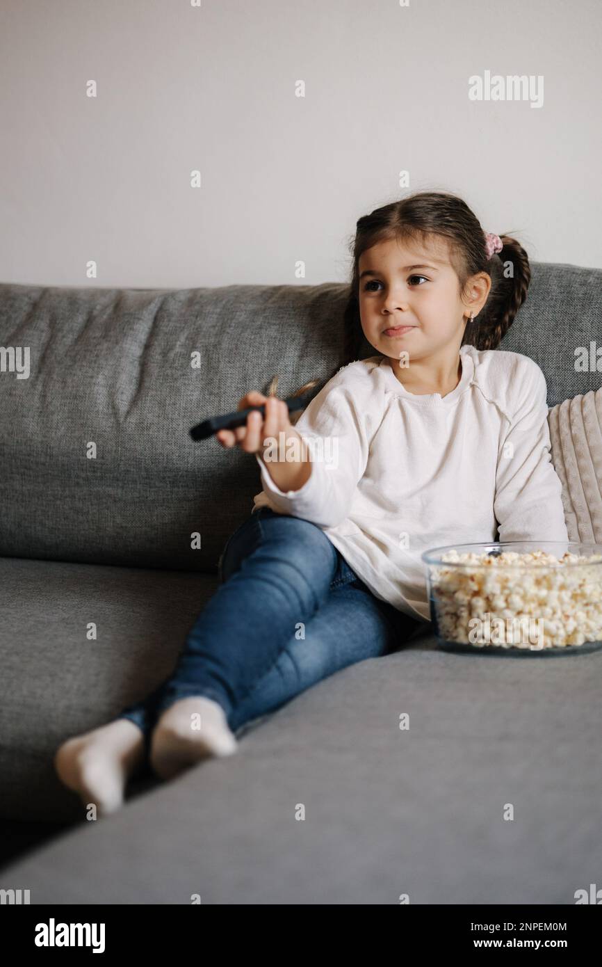 Cute little girl using remote controller of TV and watching cartoons ...