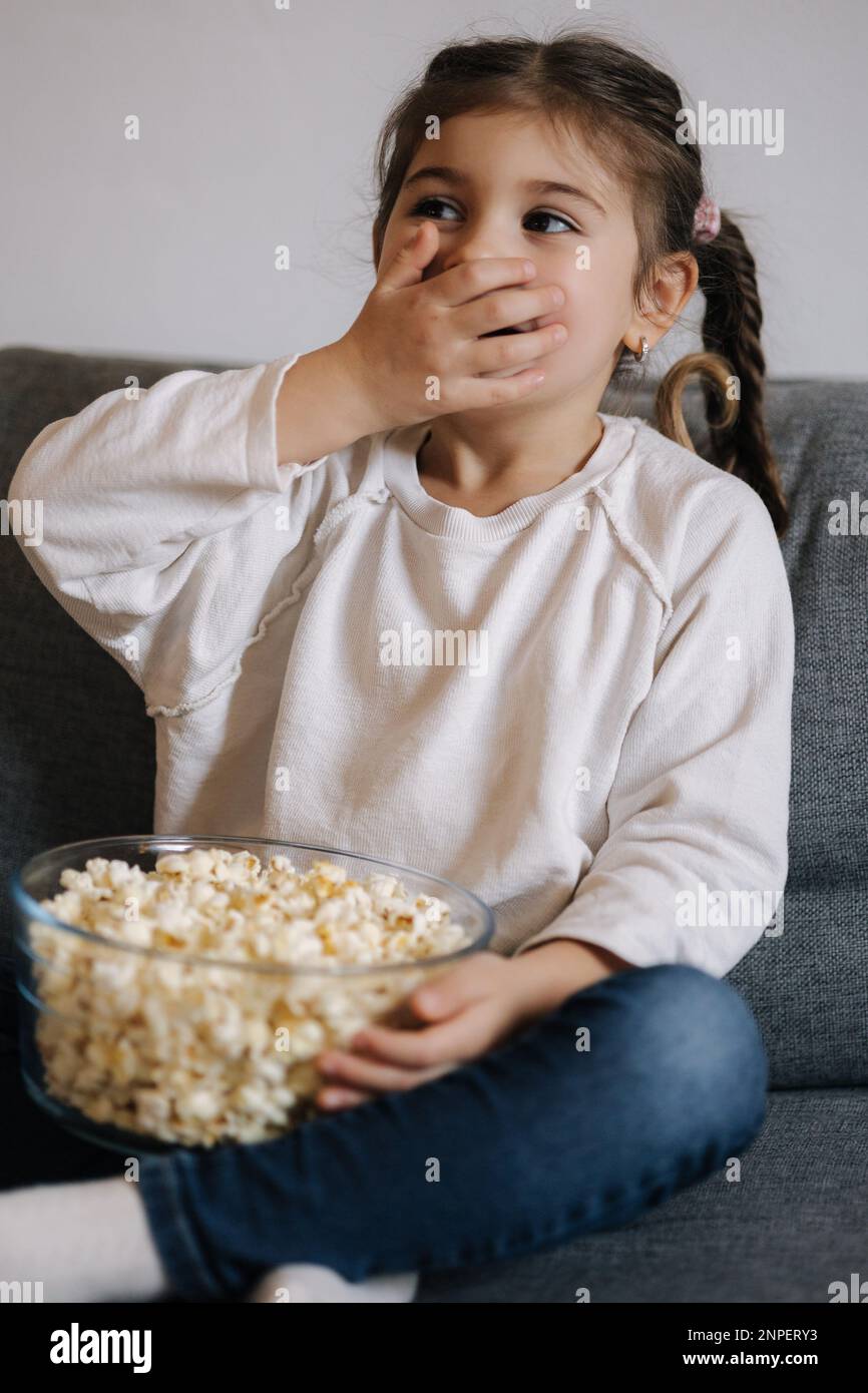 Little girl watching a cartoon emotionally and covers her mouth with ...