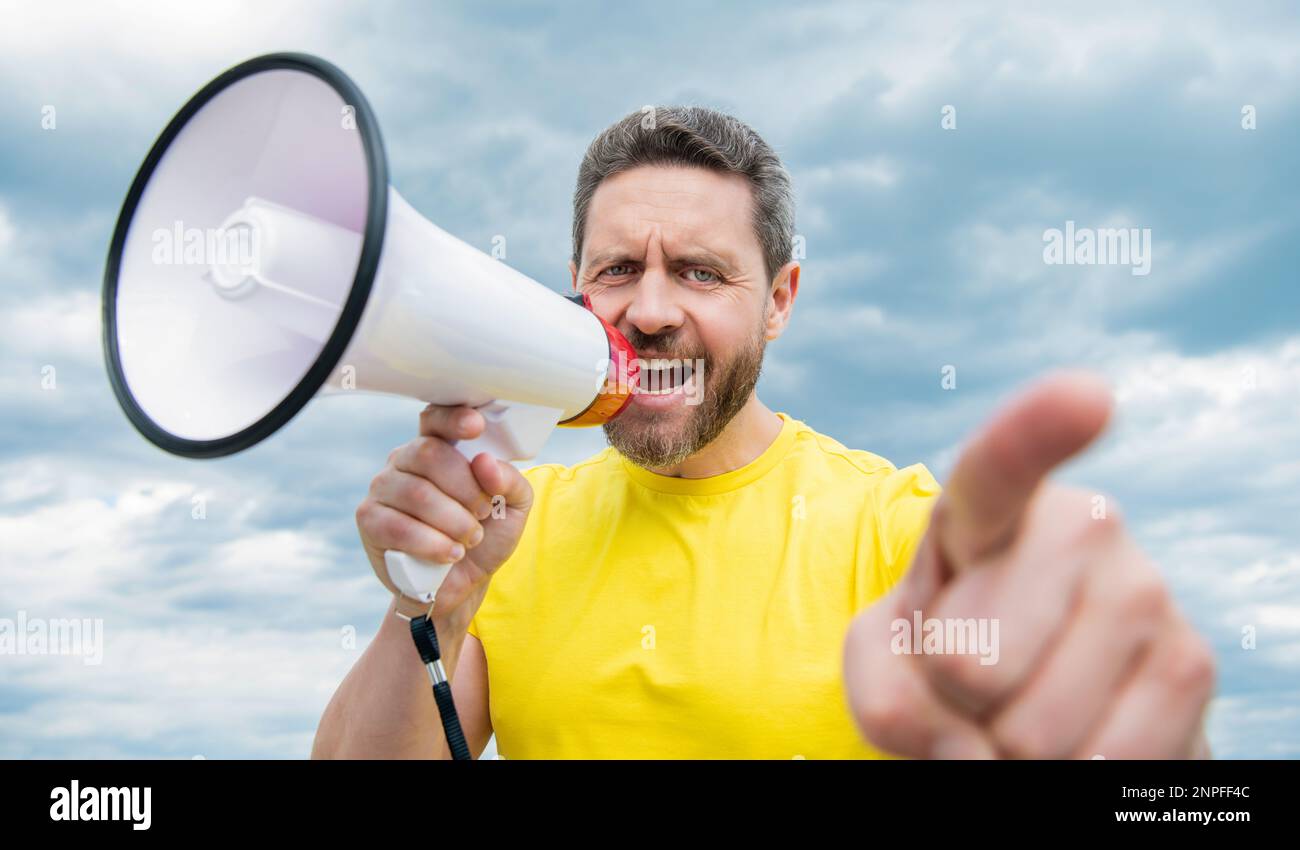 man in yellow shirt shout in loudspeaker on sky background. attention ...