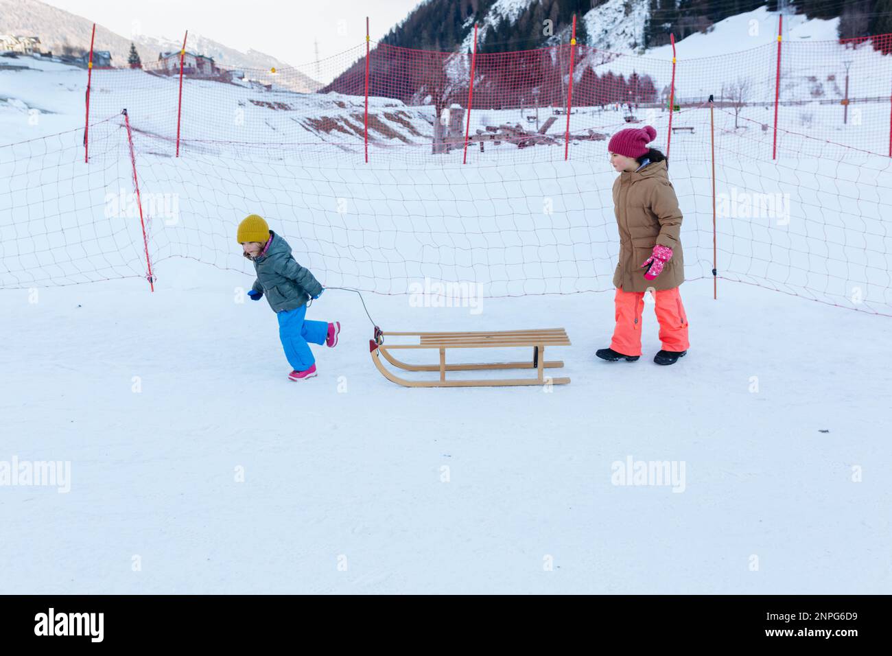 two children in ski pants pulling the wooden sledge on snow slope Stock ...