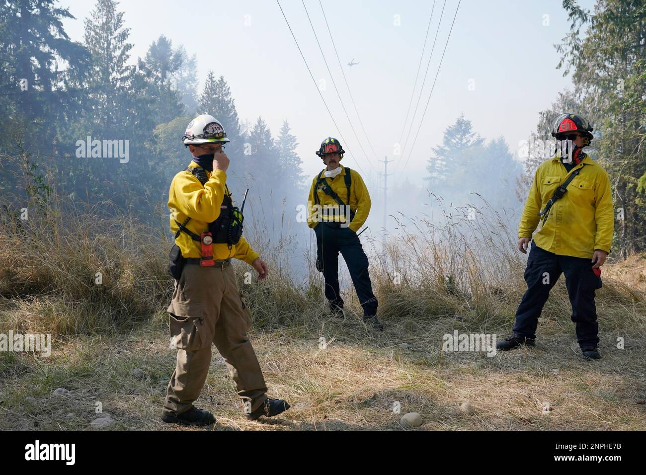 Firefighters wait under power lines for a helicopter to make a water ...