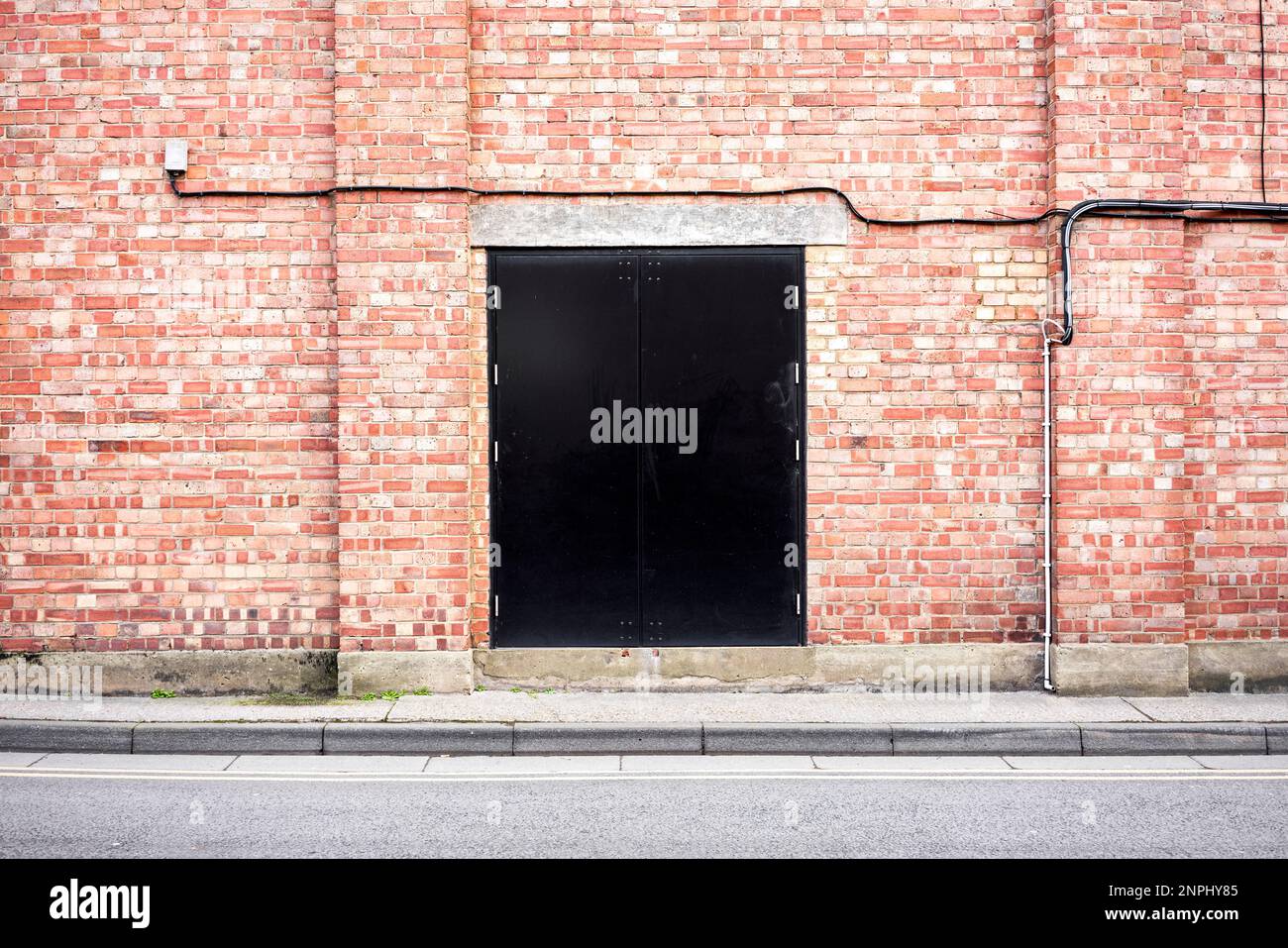 Red brick wall with black doors and cables Stock Photo - Alamy