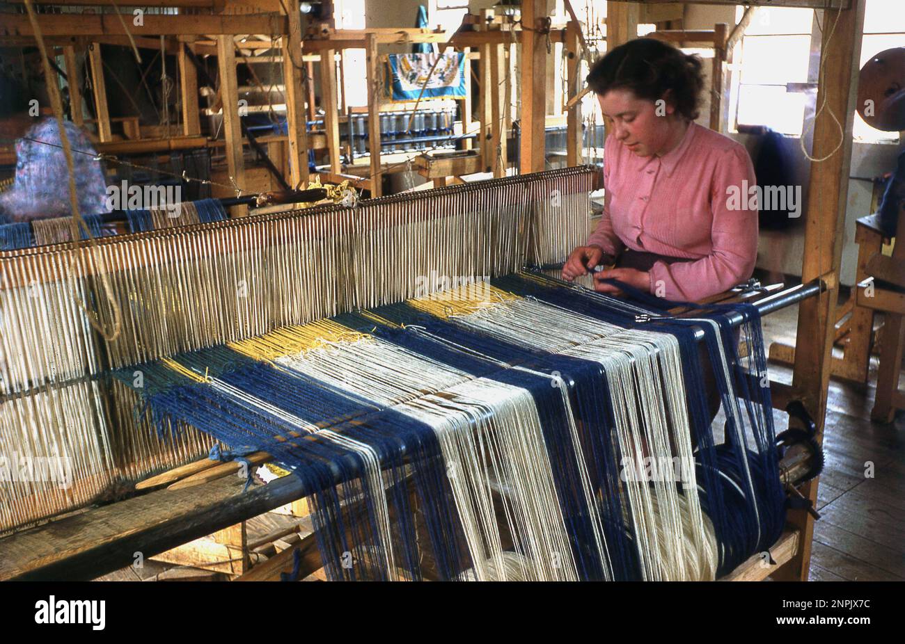 1960s, historical, inside an artisan workshop, at wooden frame loom, a lady sitting, weaving ...