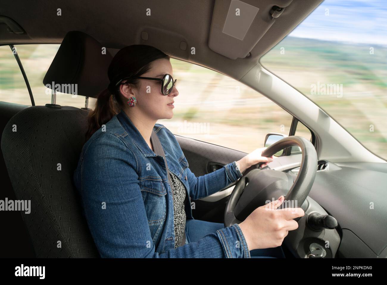 Side view of young latin woman dressed in blue with glasses driving her ...