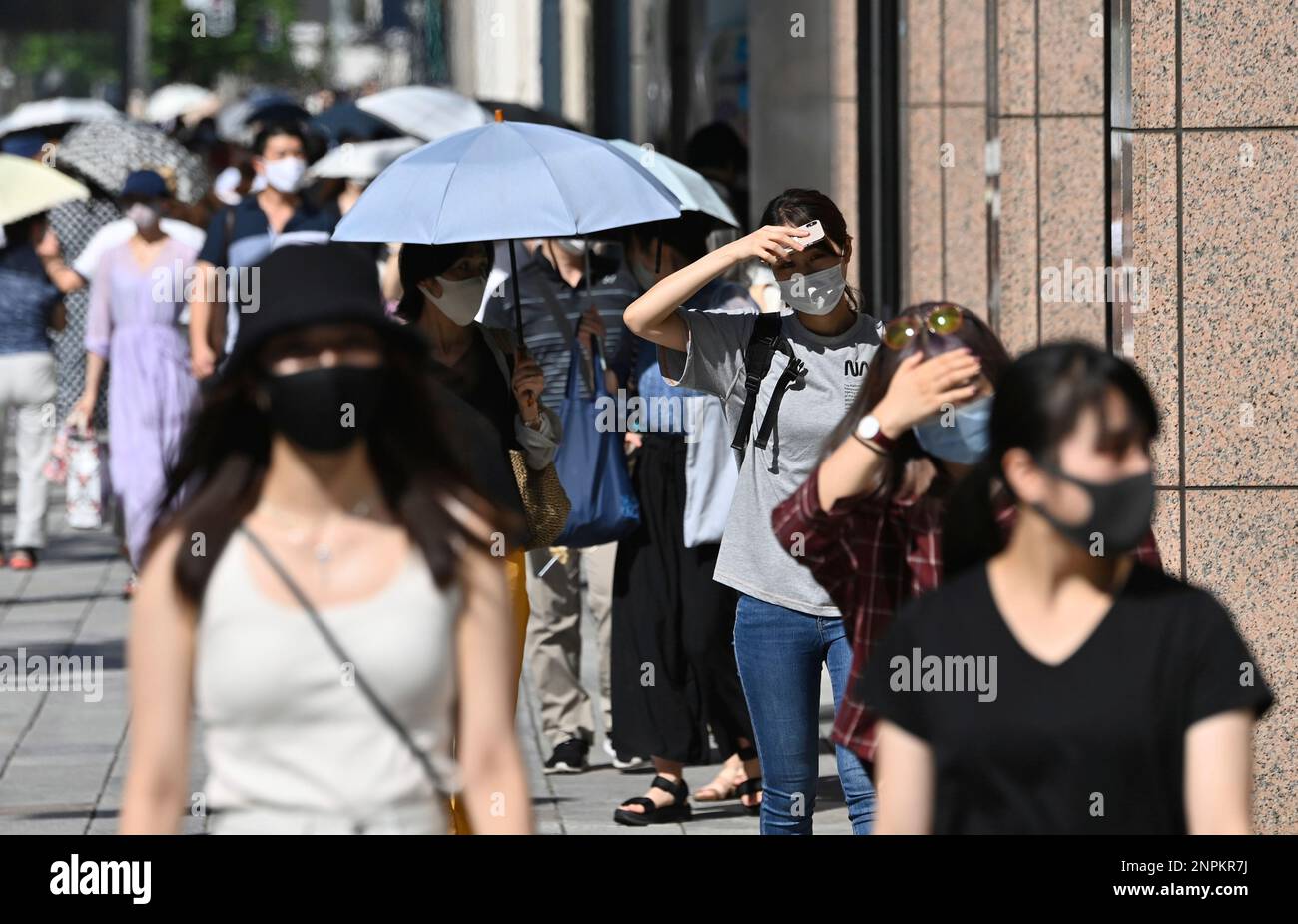 People wearing masks walk in strong sunlight at Ginza distrct in Tokyo ...
