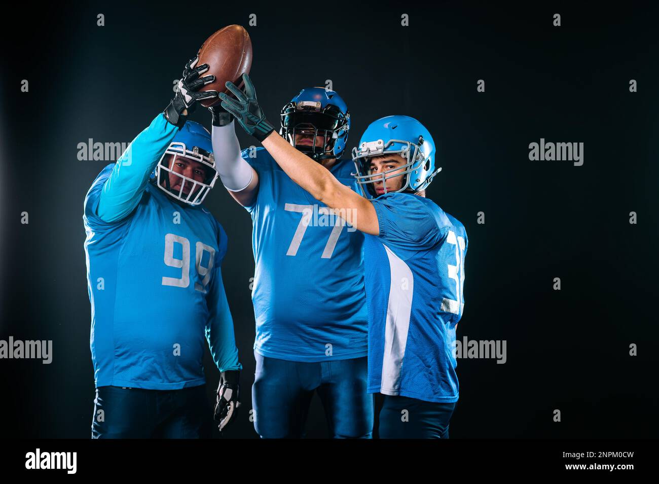 Three American football players raising their hands up holding the ball ...