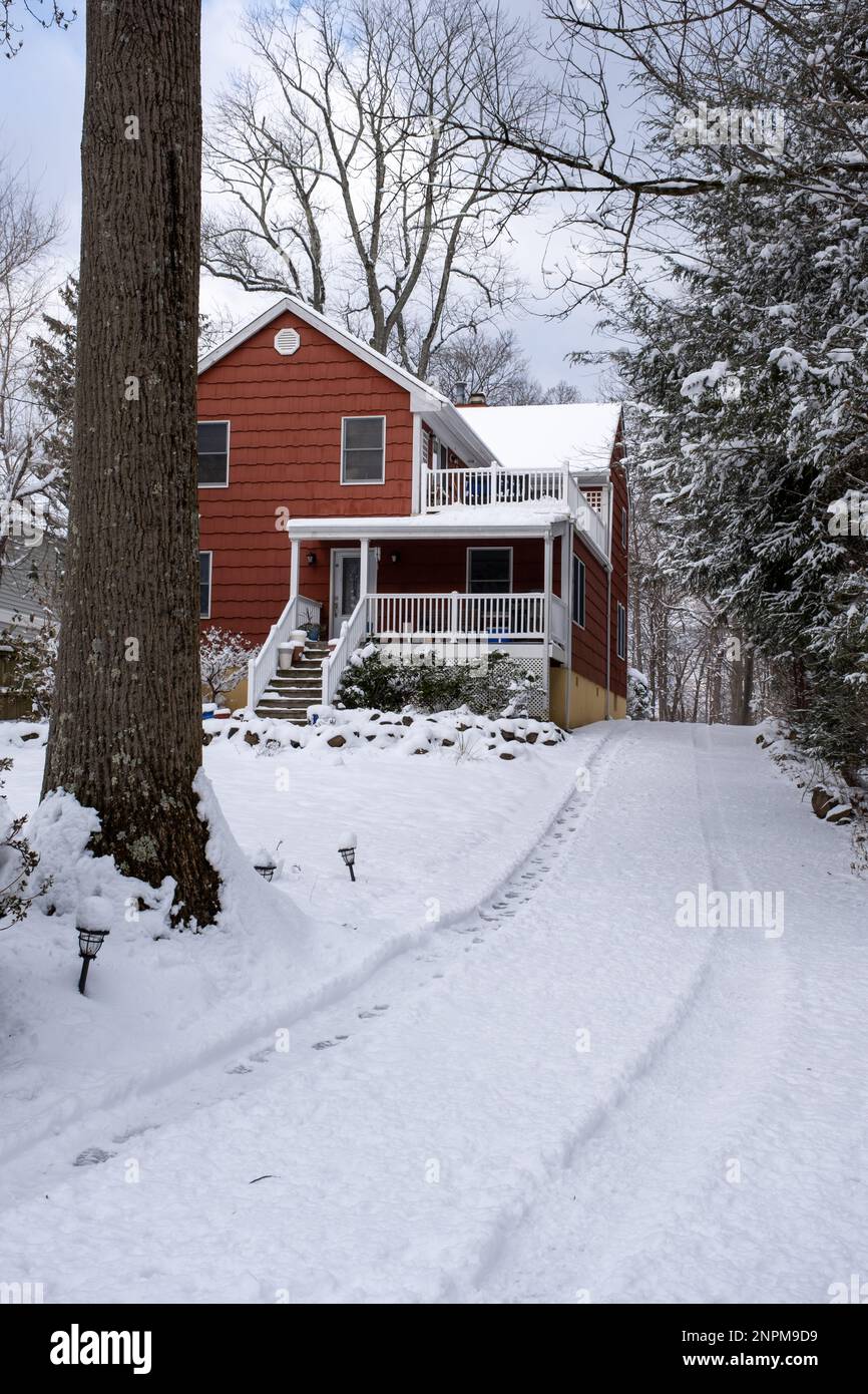 red suburban house with front yard and driveway covered with snow after ...