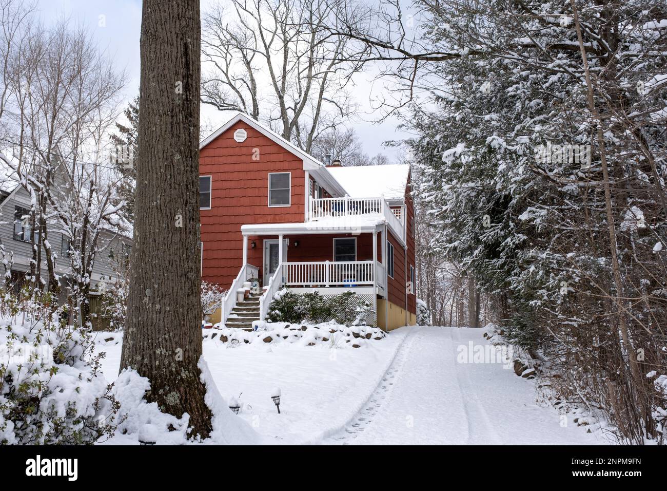 red suburban house with front yard and driveway covered with snow after ...