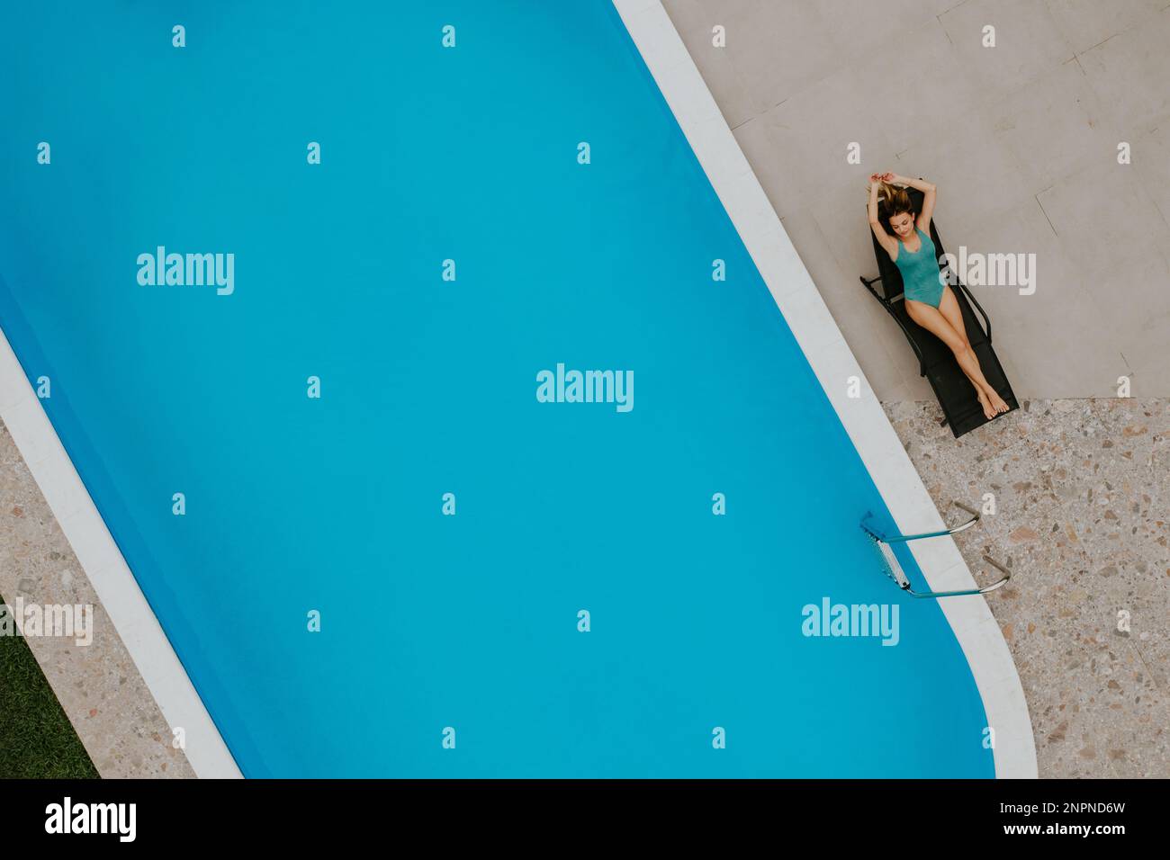 Aerial view at pretty young woman lying on a deck char by the swimming ...