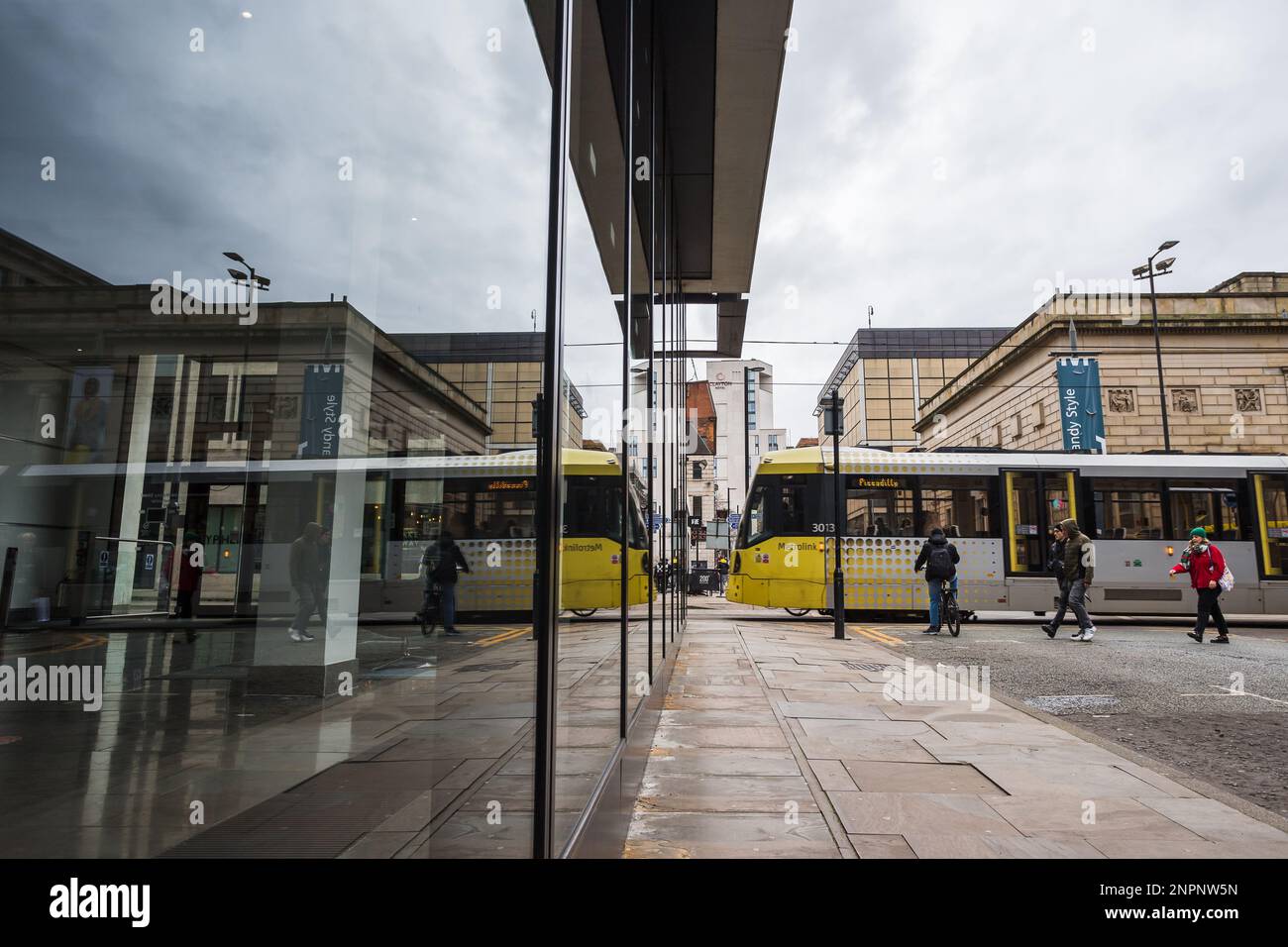 A yellow Metrolink tram reflected in the glass of a modern office ...