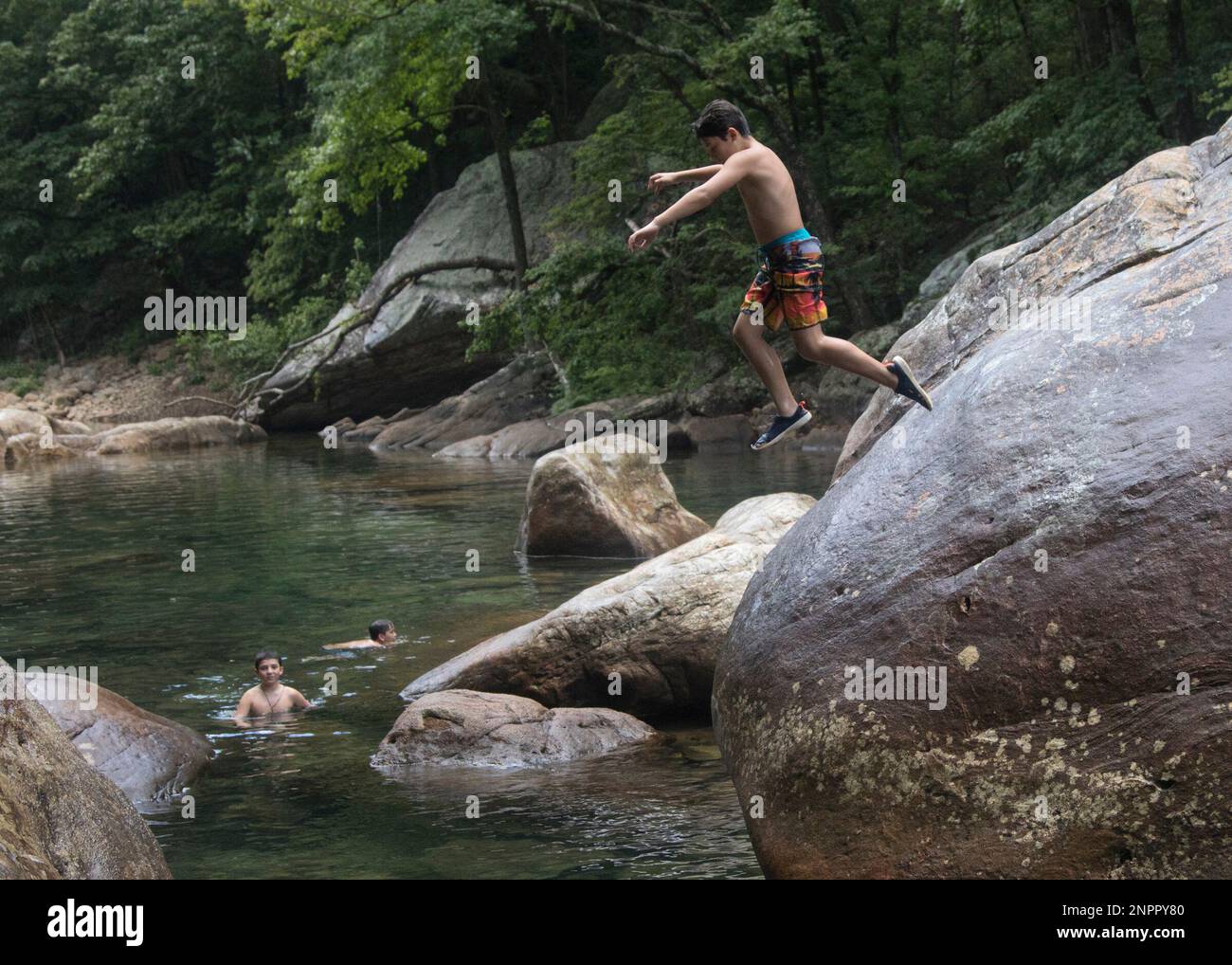 Isaiah Ardoin, 10, jumps off a rock into a swimming hole as his brother ...