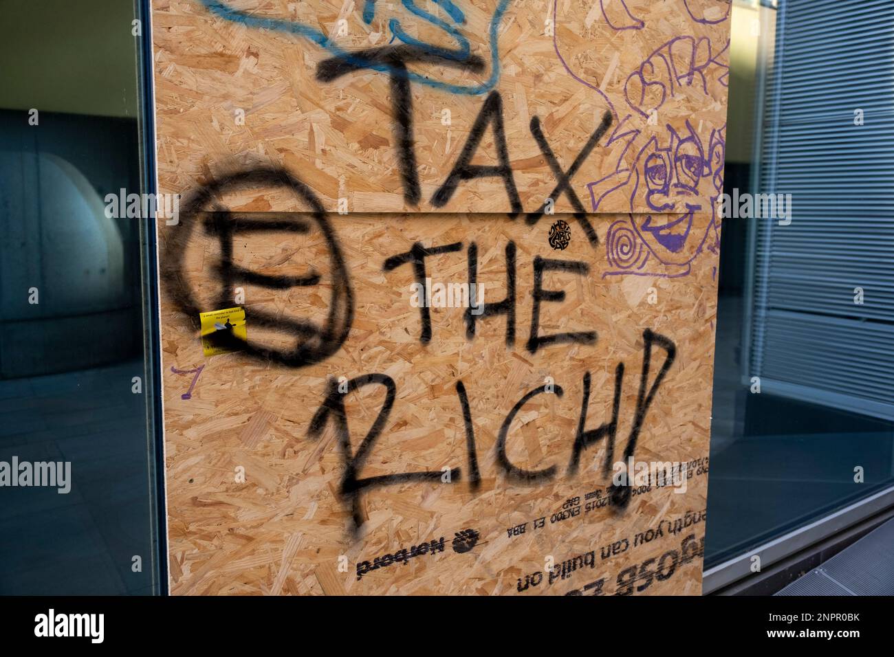 Anarchist graffiti on a boarded up window reads tax the rich relating ...