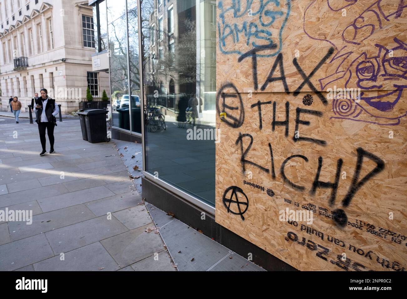 Anarchist graffiti on a boarded up window reads tax the rich relating ...