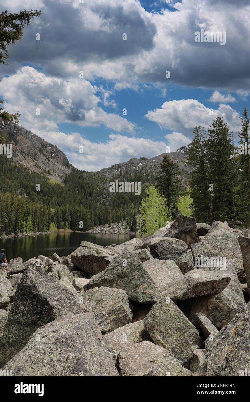 A young man sitting on a boulder looking at Weller Lake, surrounded ...