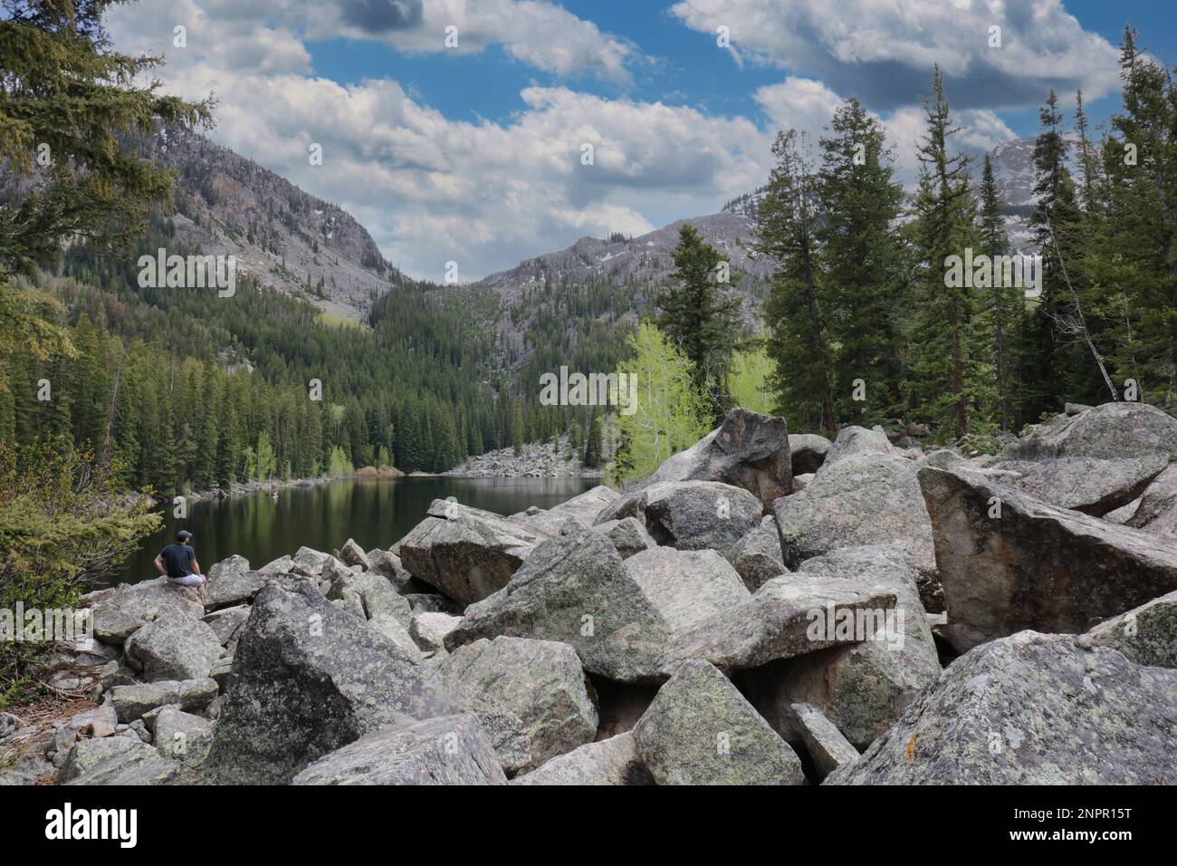 A young man sitting on a boulder looking at Weller Lake, surrounded by ...