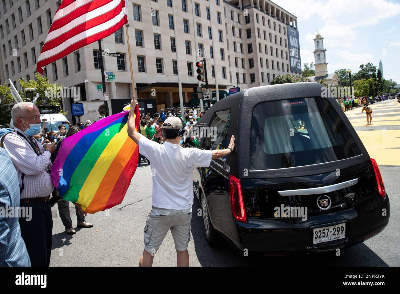 A man holding a pride and American flag touches the hearse with the ...