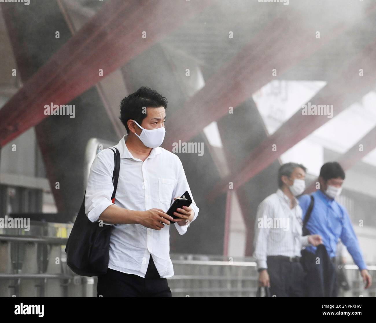 People wearing face mask walk in the mist spray in front of JR Gifu station in Gifu on July 20 ...