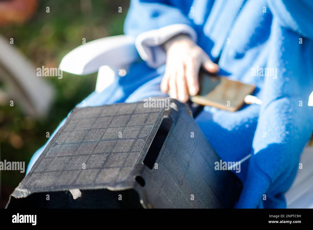 A portable solar battery rests on the legs of an unrecognizable woman ...
