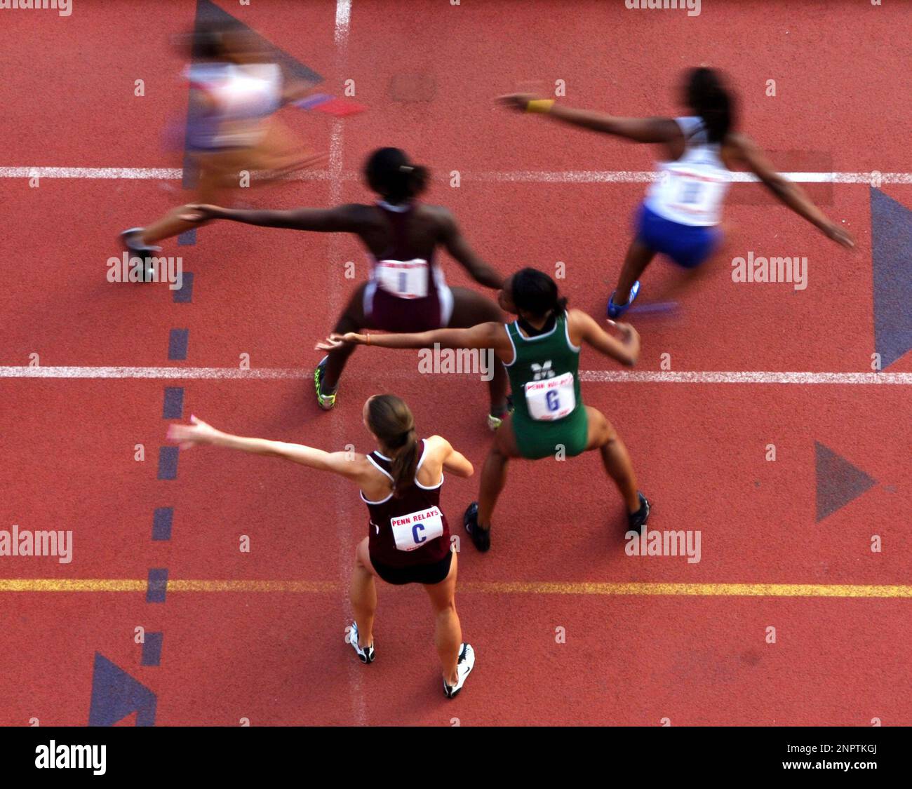 Runners hand off batons in the exchange zone of the college women's 4 x ...