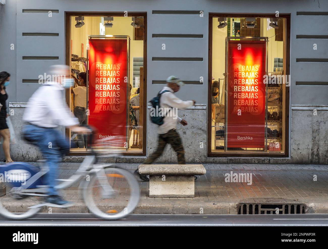 Several people pass by the window of a shop where signs indicating ...