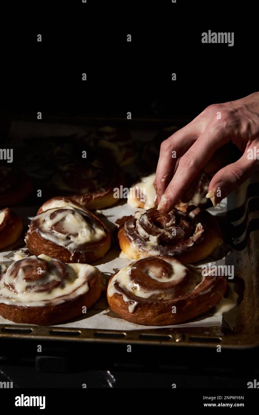 Cinnabon rolls on black background. Hand touches cinnabon from the top ...