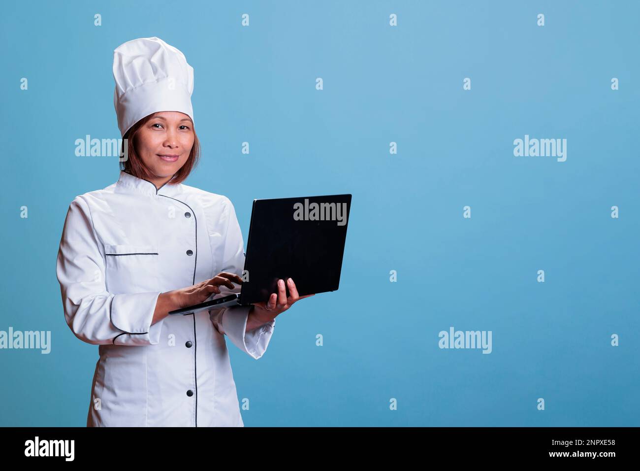 Cheerful cook with apron holding laptop computer checking gastronomy ...
