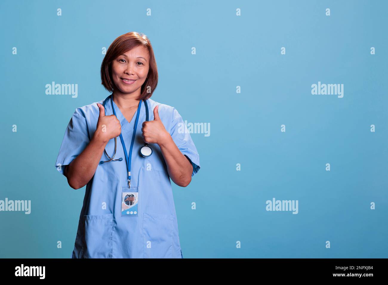 Smiling physician nurse wearing medical uniform over blue background ...