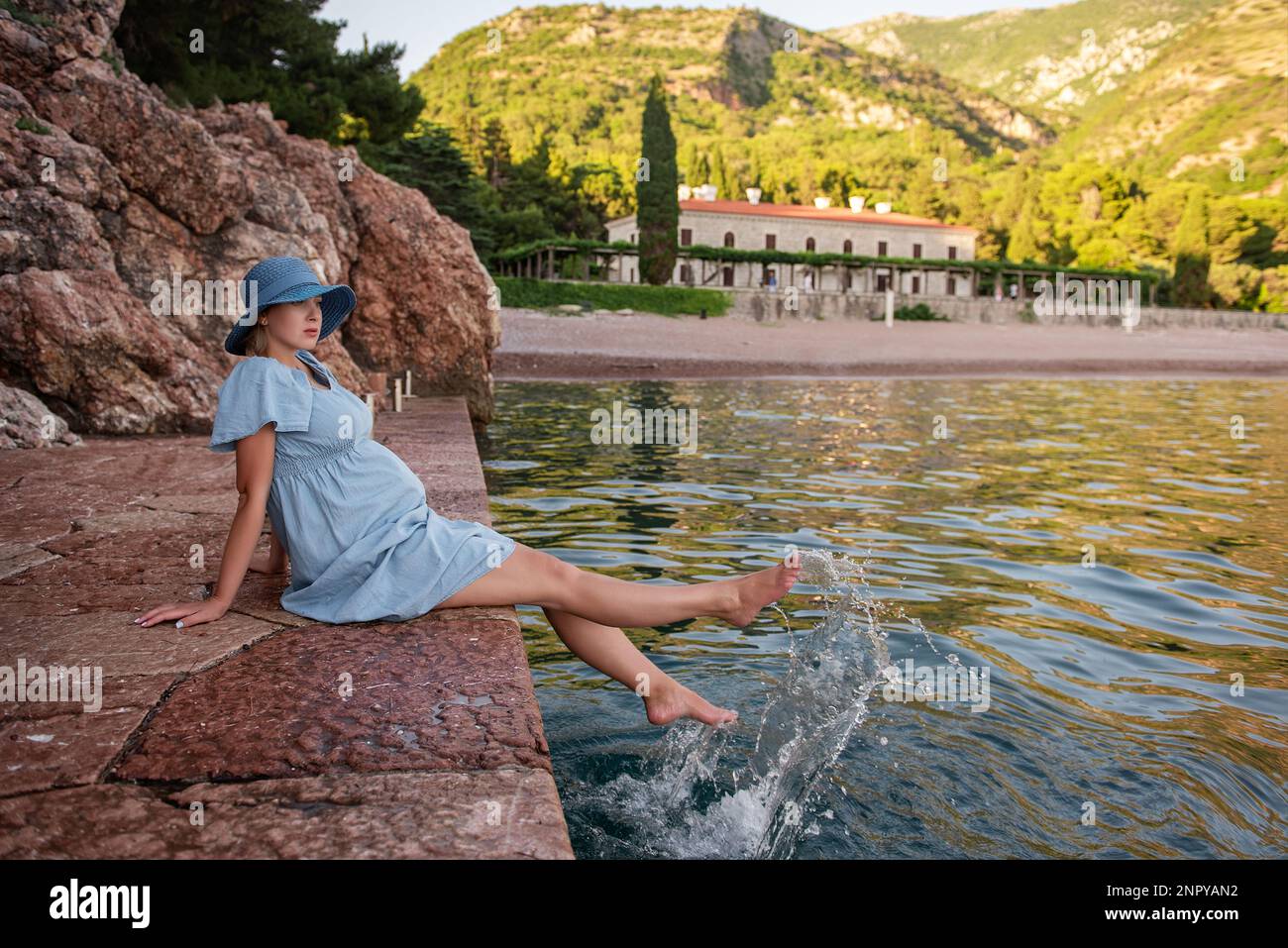 Pregnant woman traveler in denim dress, blue straw hat sits by the sea ...