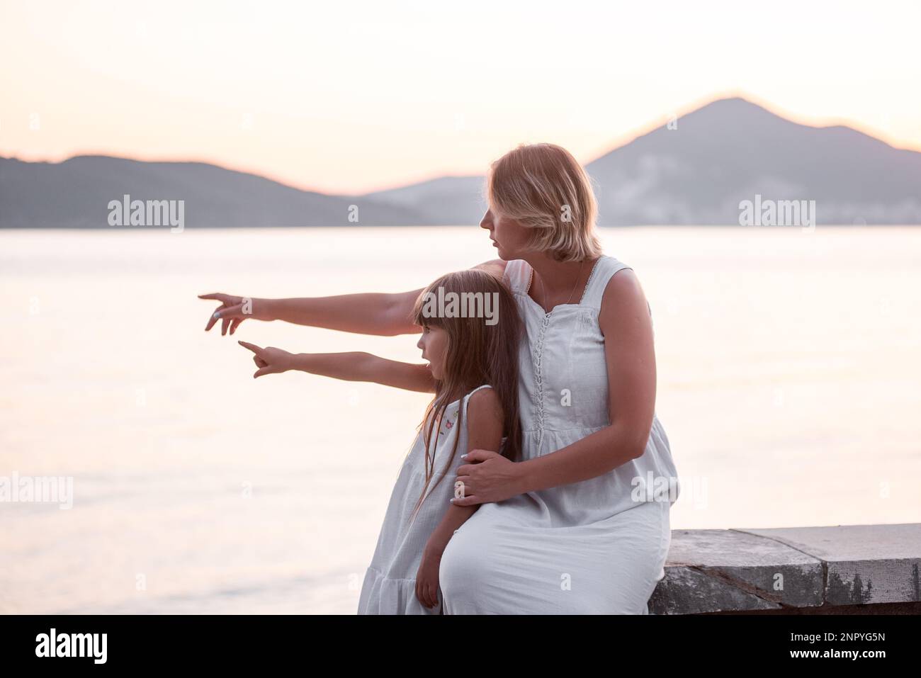 Pregnant Millennial Mother sit with daughter at sunset by the sea ...