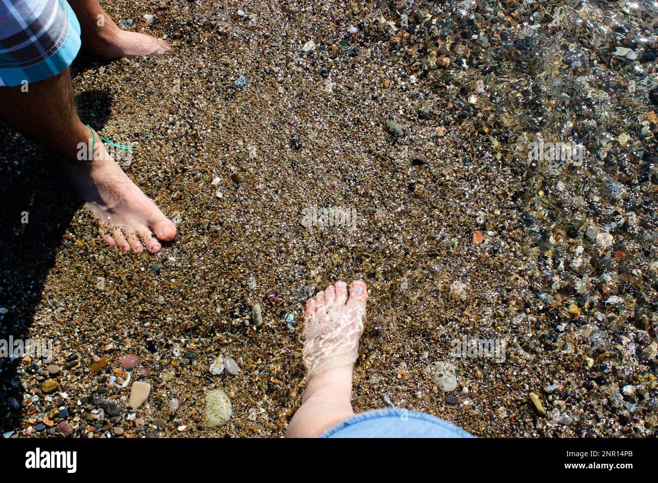 Two Caucasian people have their feet dipped in a water source with sand ...