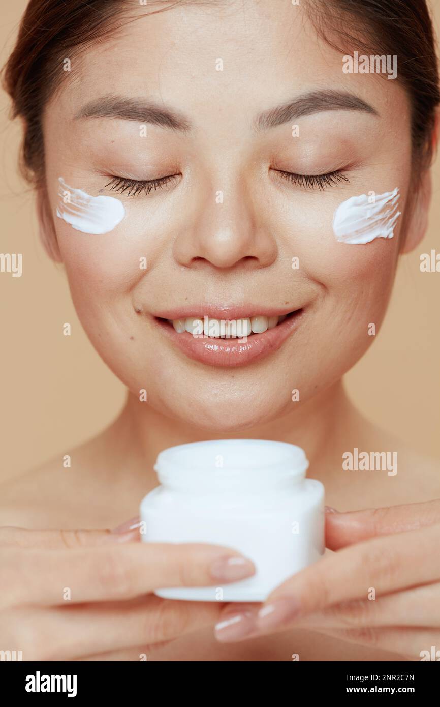 modern woman with facial cream jar and facial cream on face on beige ...