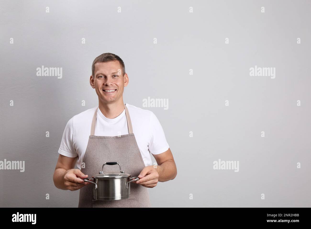 Happy man with cooking pot on light grey background. Space for text ...