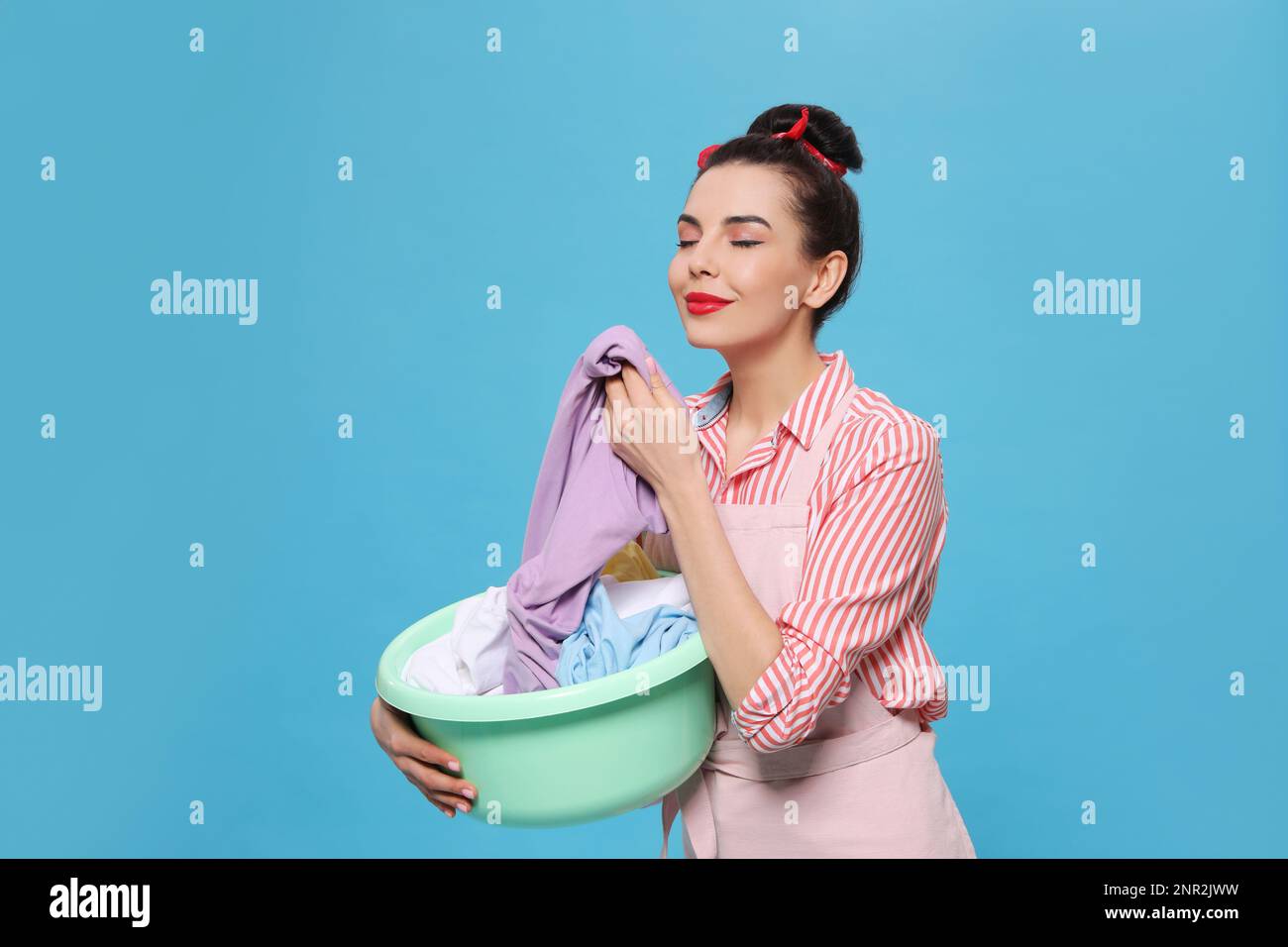 Housewife holding basin with clothes on light blue background Stock ...
