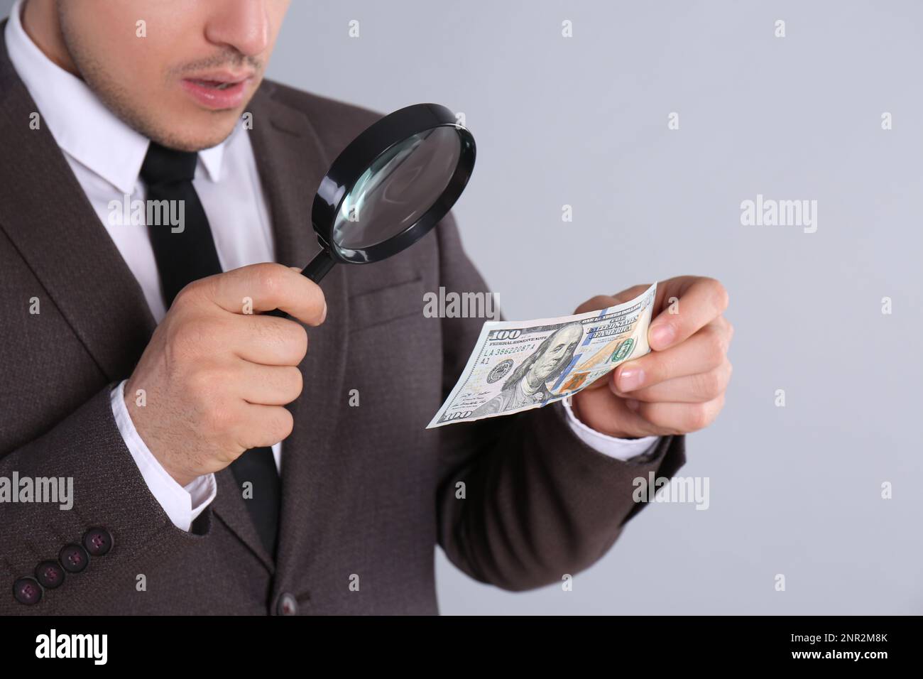 Expert authenticating 100 dollar banknote with magnifying glass on ...
