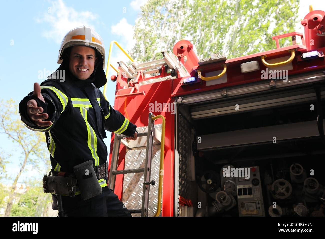 Firefighter in uniform and helmet offering hand near fire truck ...