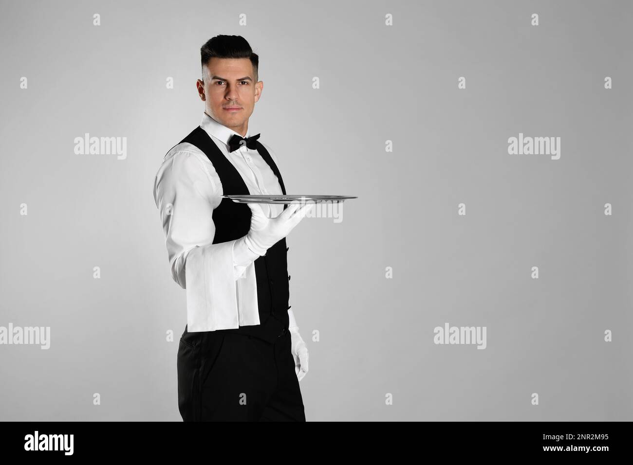 Handsome butler with tray on light grey background, space for text ...